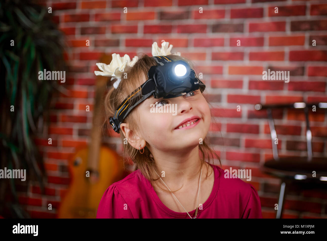 A little girl wearing a flashlight on his head and stands on brick wall ...