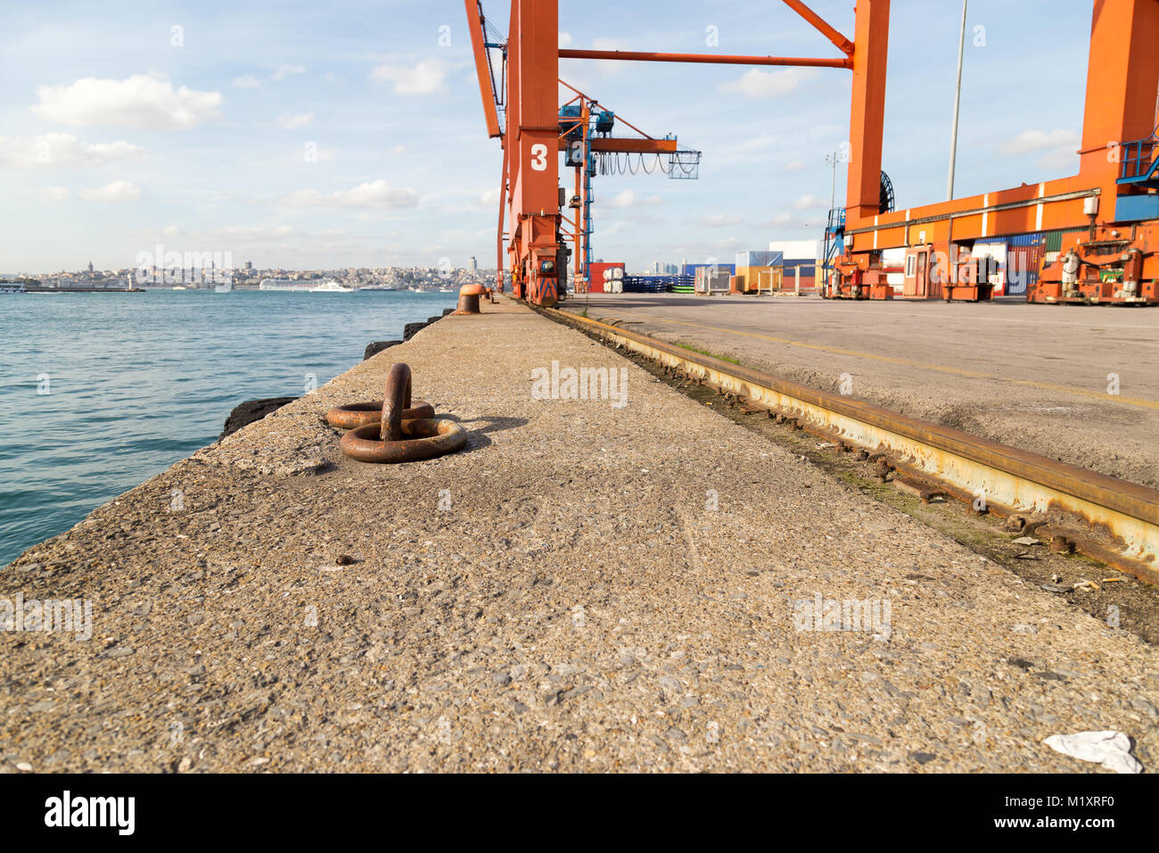 Old iron bollard over the stone dock with near the blue sea and crane ...