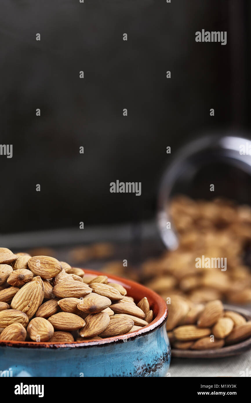 Whole almonds in bowl and wooden spoon against a rustic background ...