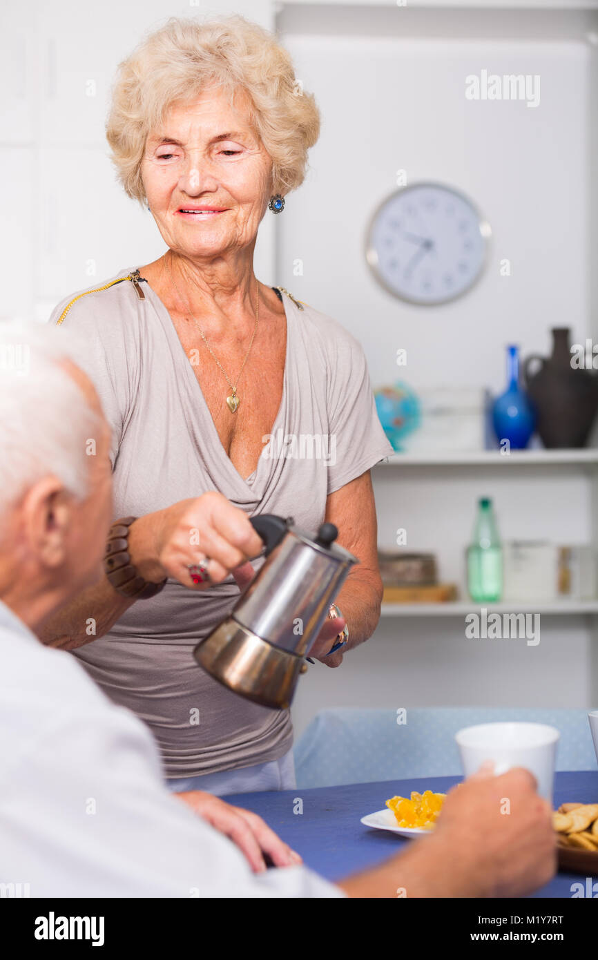 Happy senior woman pouring tea into cup during breakfast with husband ...