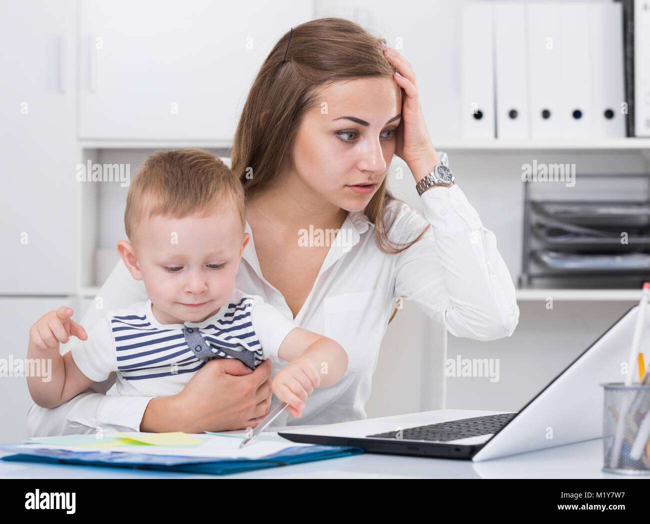 Perplexed mother with kid is having issue while working behind laptop ...