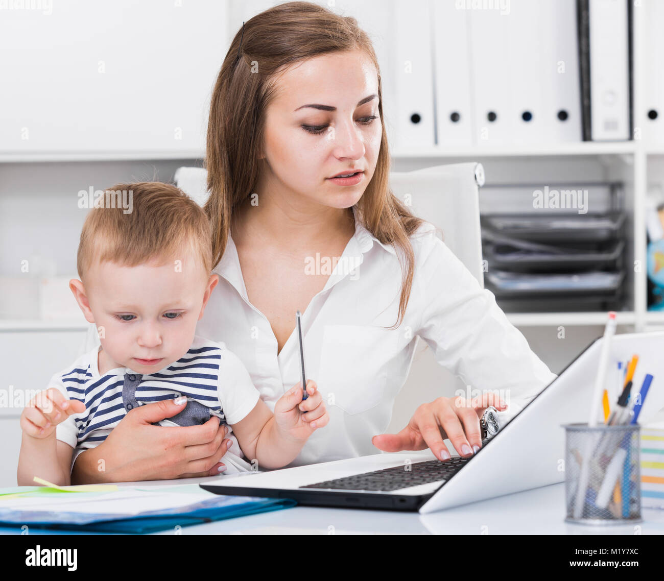 Mother with kid is working behind laptop in office Stock Photo - Alamy