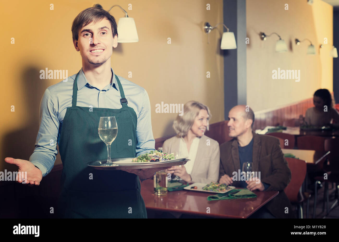 Portrait of waiter working in ordinary restaurant and holding tray ...