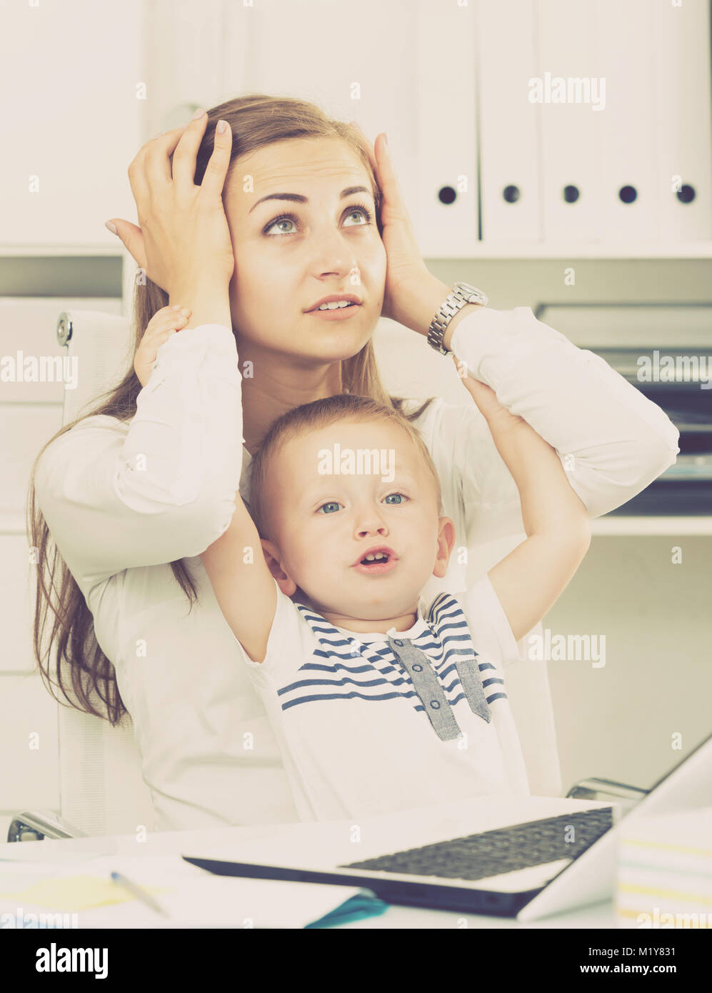 Perplexed girl with kid is having issue while working behind laptop in ...
