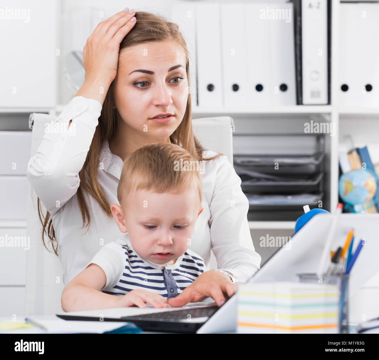 Perplexed girl with child is having problems while working in office ...