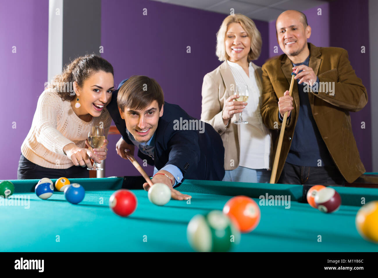 Two joyful smiling couples having pool game in billiard club ...
