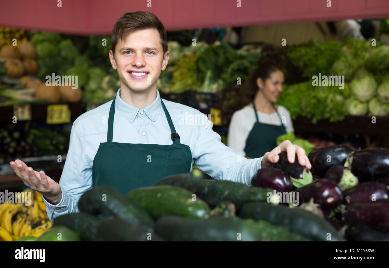 smiling european stuff in apron selling green cucumber at marketplace ...