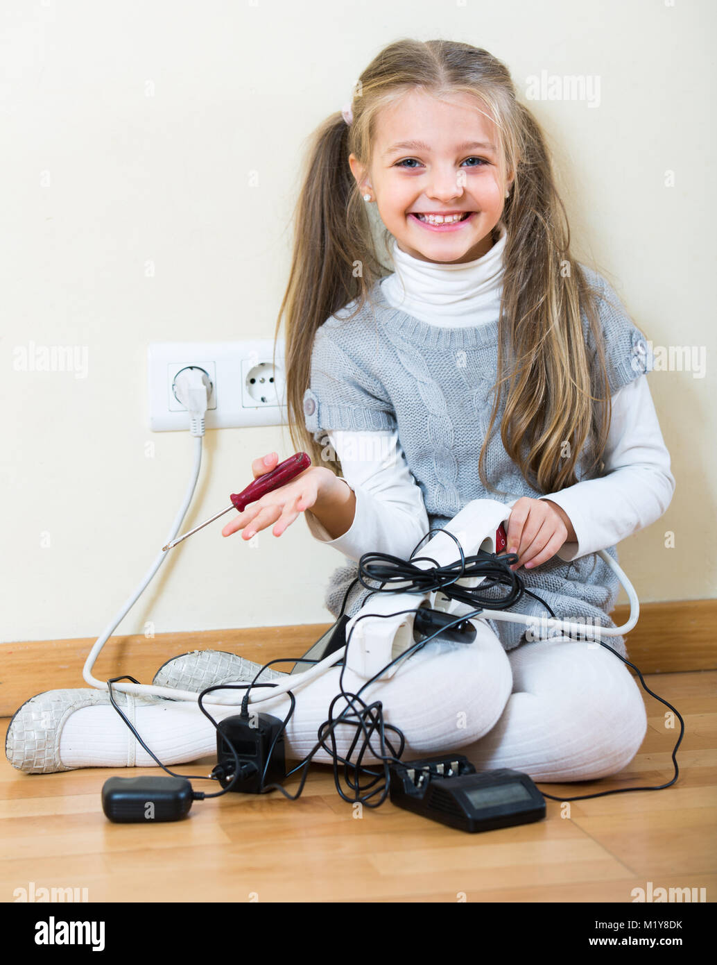 Cheerful little girl dangerously playing with sockets and electricity ...