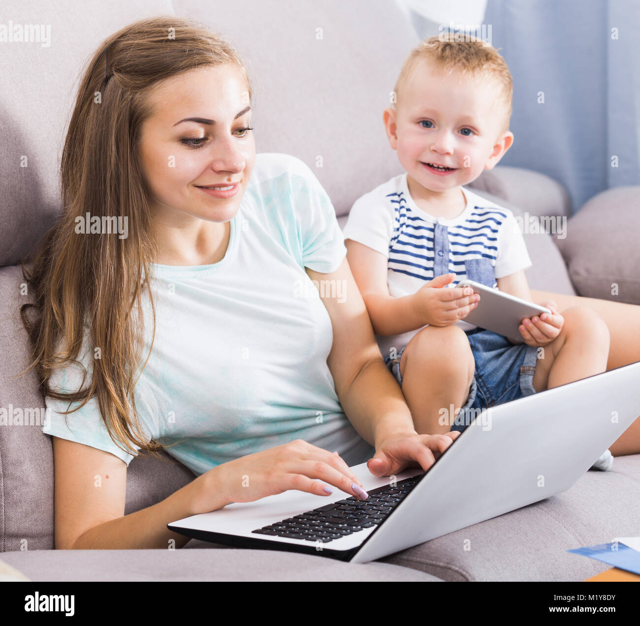 Smiling mother is productively working behind laptop while child ...