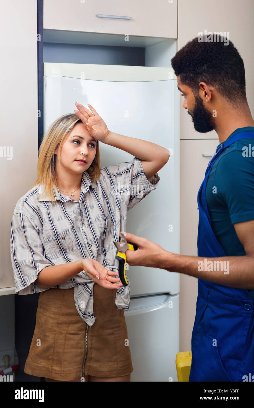 Upset young woman complaining to black handyman on problems with fridge ...