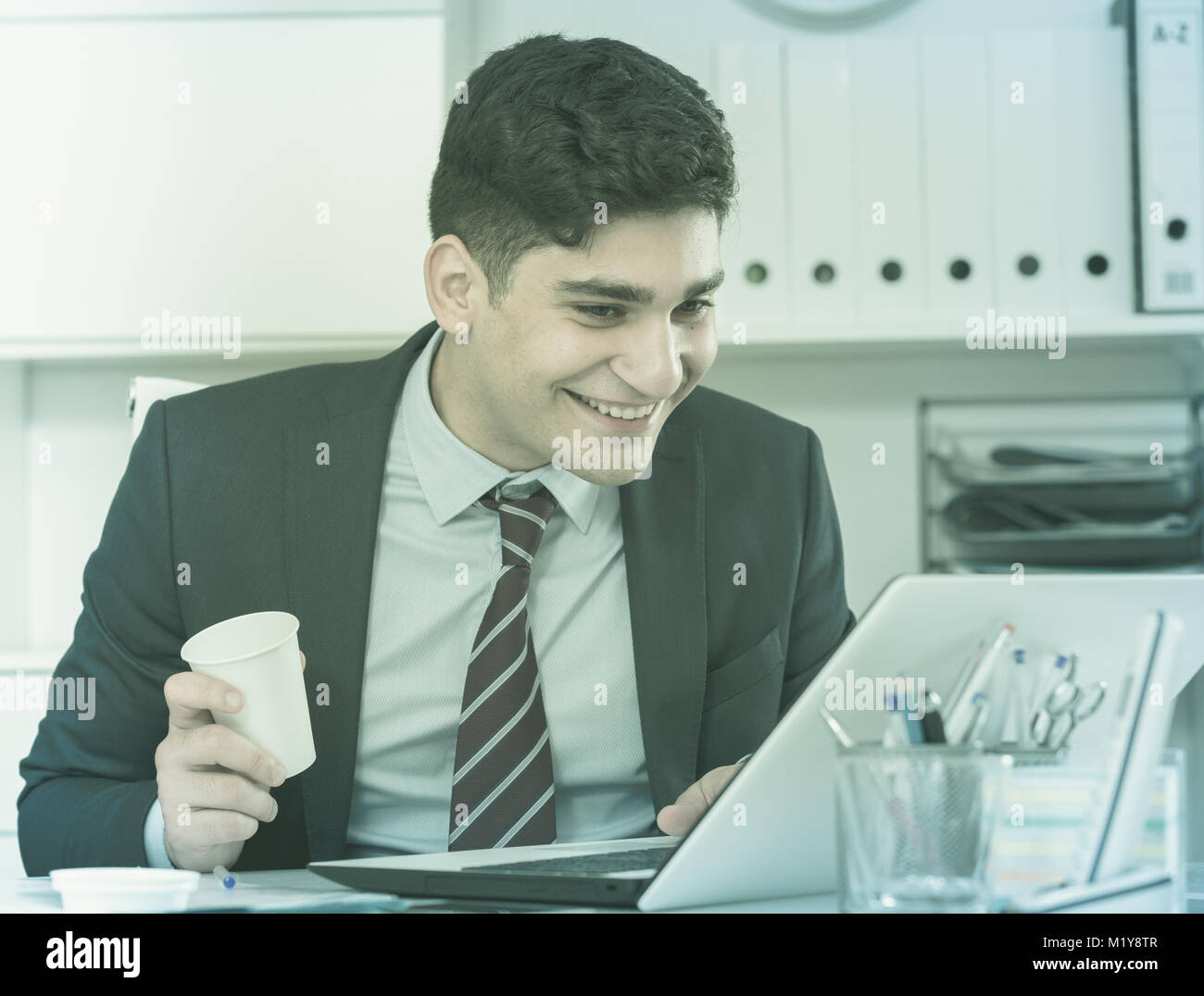 Adult businessman is working at a computer and drinking coffee in the ...