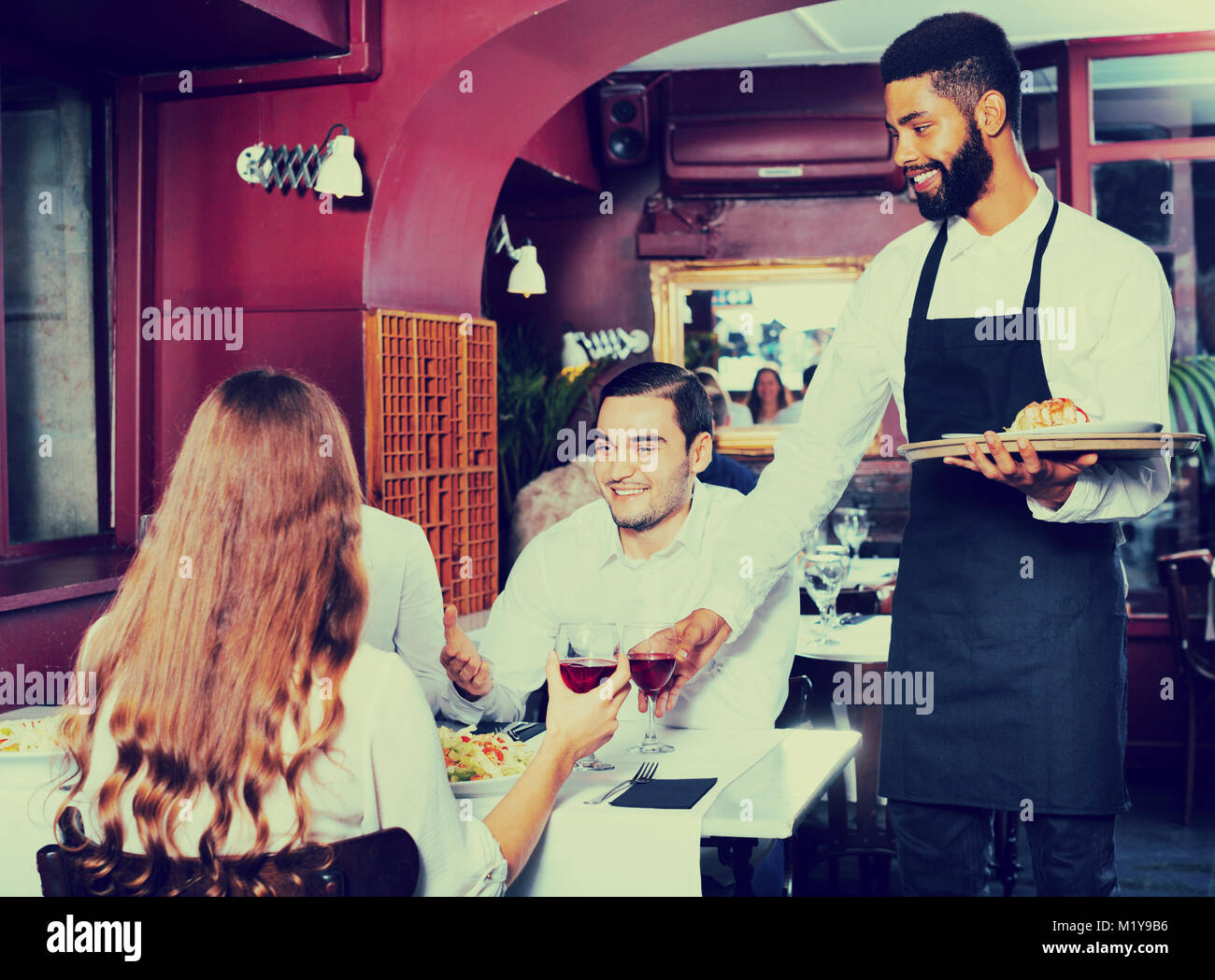 Smiling young waiter taking care of adults at cafe table Stock Photo ...