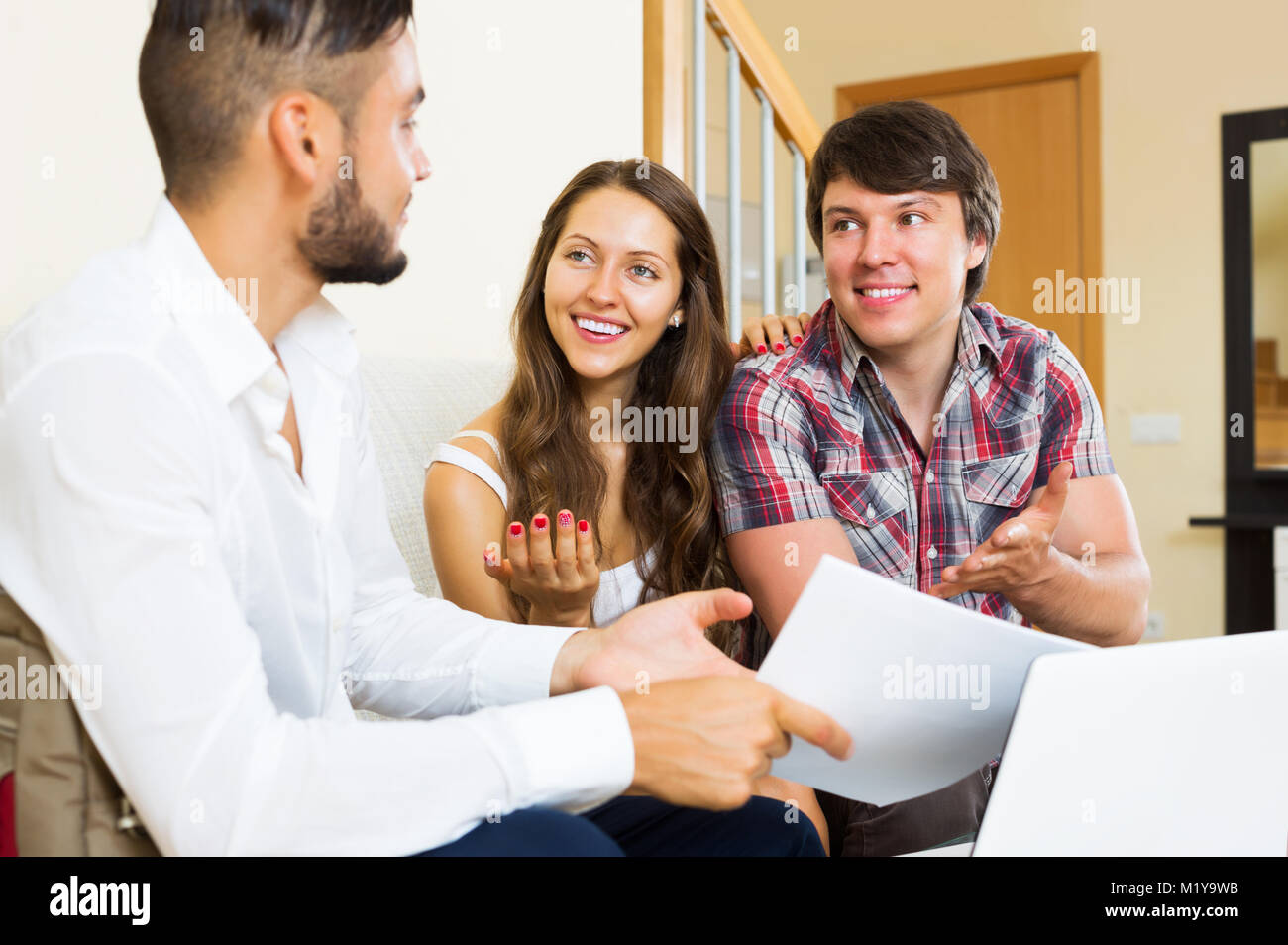 Happy young couple and salesman talking cheerfully about purchase at ...