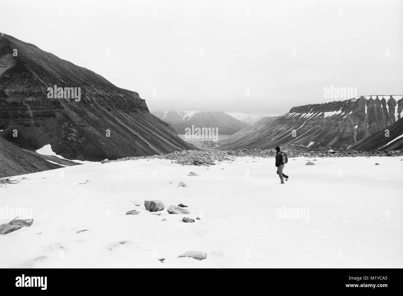 A man walking across the snow, looking down the valley towards ...
