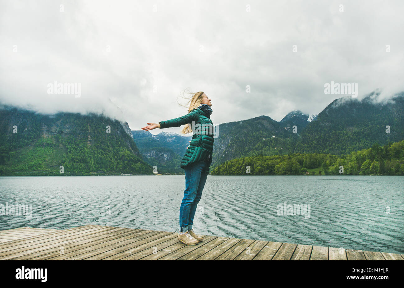 Relaxed female traveller with her arms open, standing at mountain lake ...