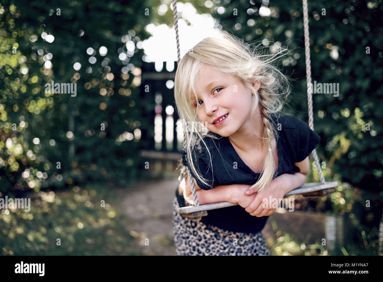 Cute little blonde girl smiling while playing alone on a swing in her ...