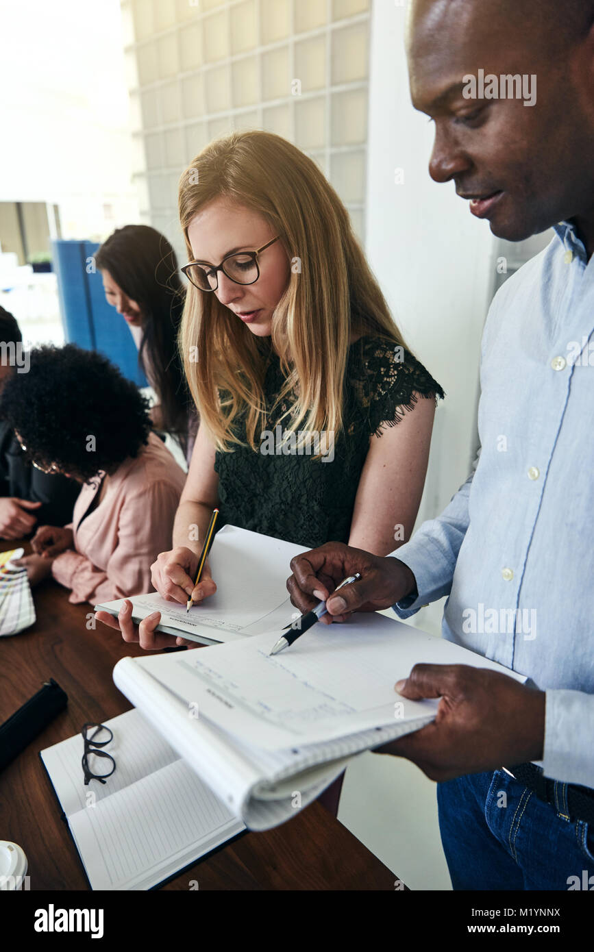 Two focused colleagues comparing notes while standing together in a ...