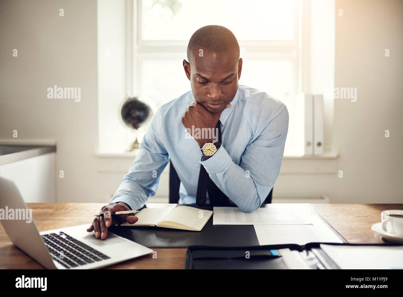 Young African executive reading documents and working on a laptop while ...
