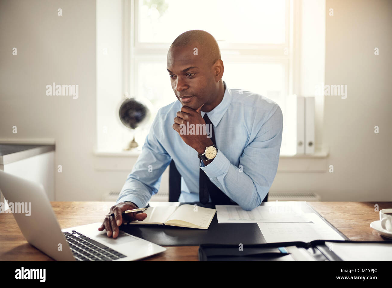 Young African business executive wearing a shirt and tie sitting at his ...