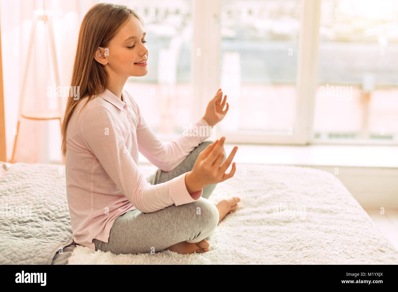 Side view of teenage girl meditating on bed Stock Photo - Alamy