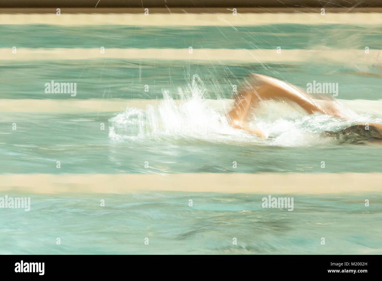 A swimmer swims the freestyle stroke at a swim meet. A slow shutter ...