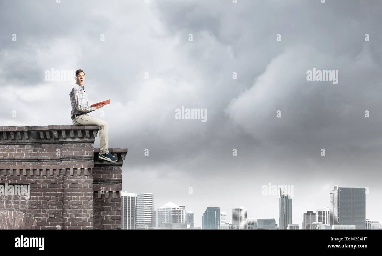 Man on roof edge reading book and cityscape at background Stock Photo ...