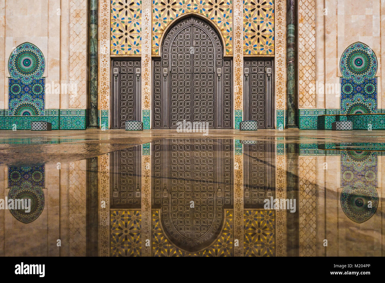 view of Hassan II mosque's big gate reflected on rain water ...