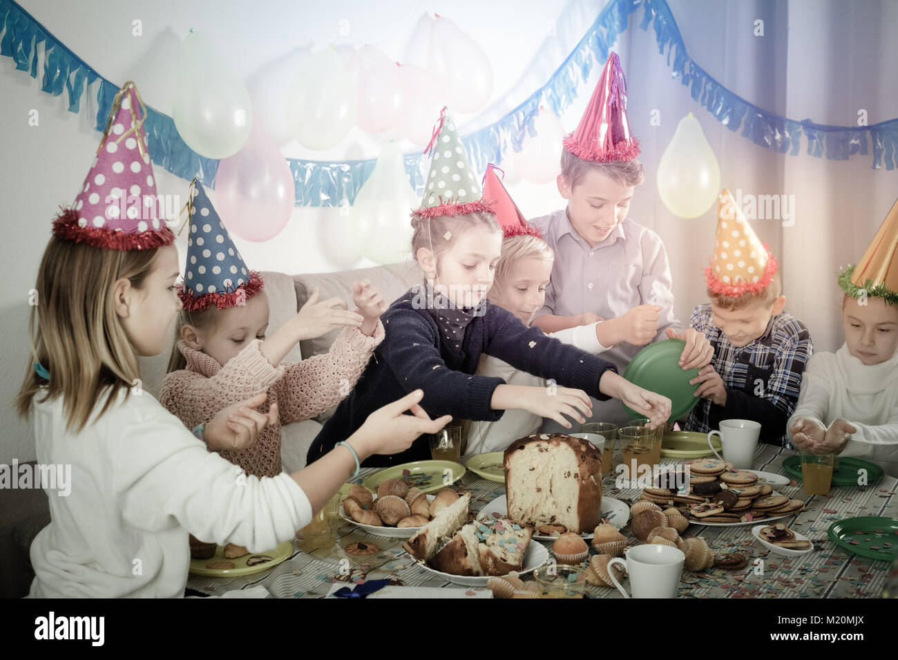 Cheerful children happy to eat and drink at friend’s birthday party ...