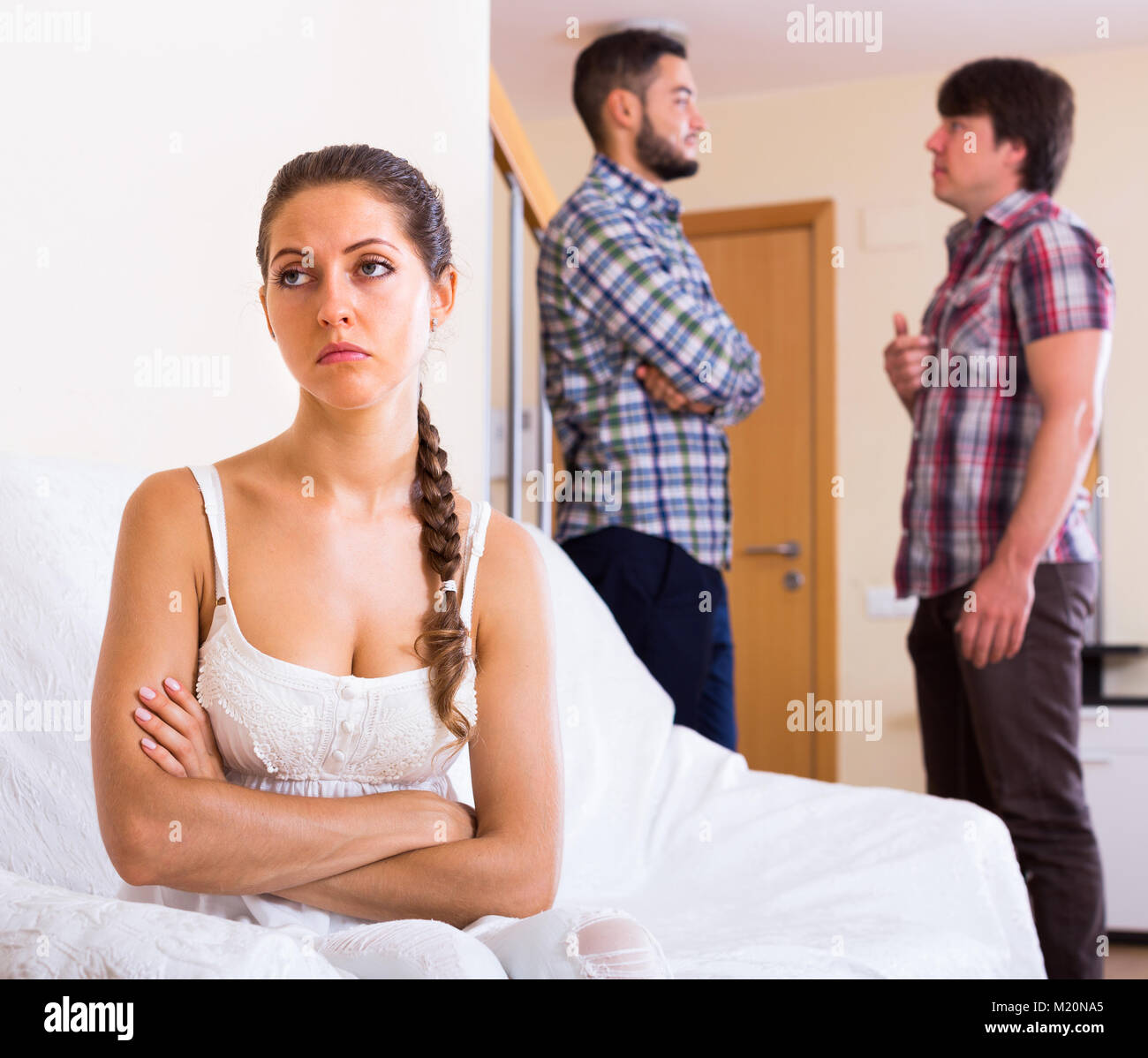 Sad girl and two angry guys at home: problems of love triangle Stock ...