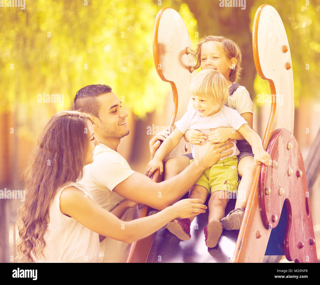 Smiling parents helping girls on slide in summer day Stock Photo - Alamy