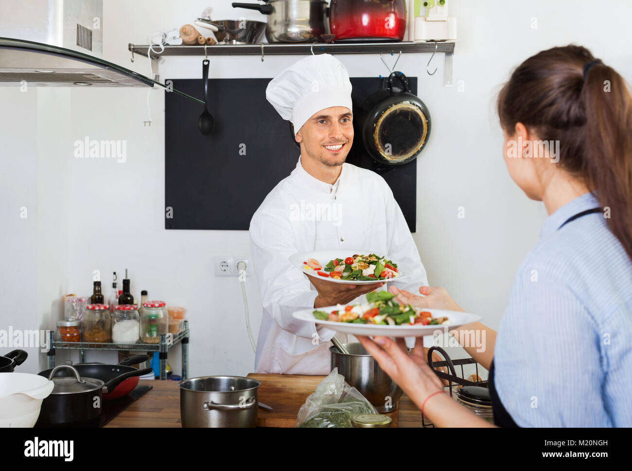 Portrait of glad young smiling man cook giving to waitress ready to ...