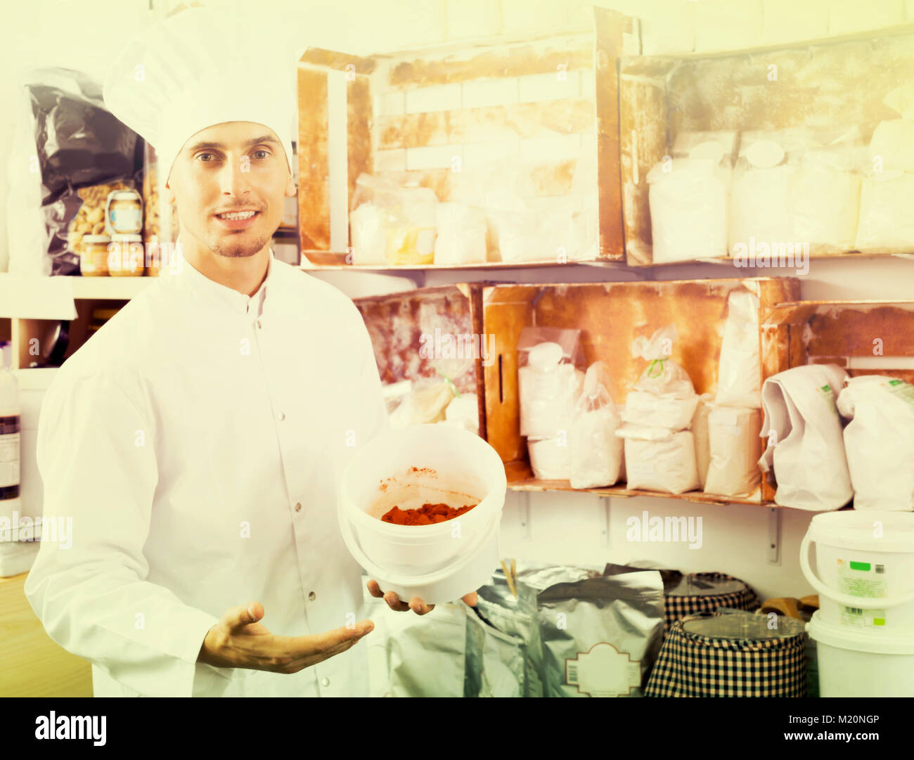 Cheerful young man chef wearing uniform holding various flour in rooms ...
