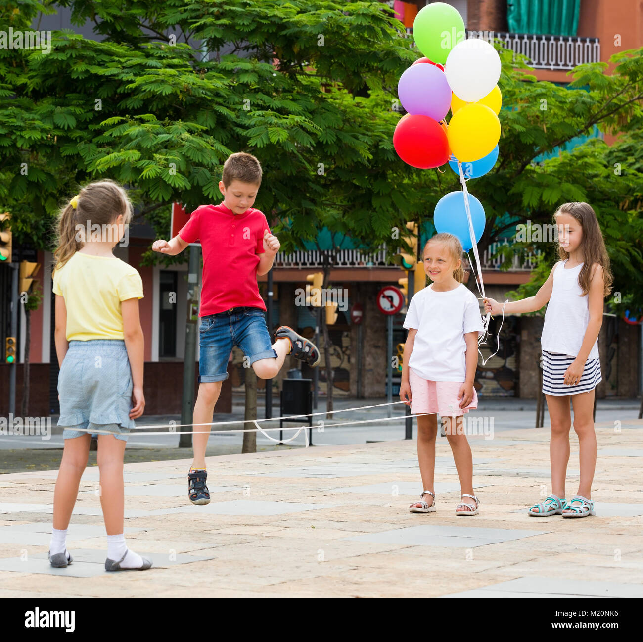 Boy skipping on chinese jumping rope and girls standing around with ...