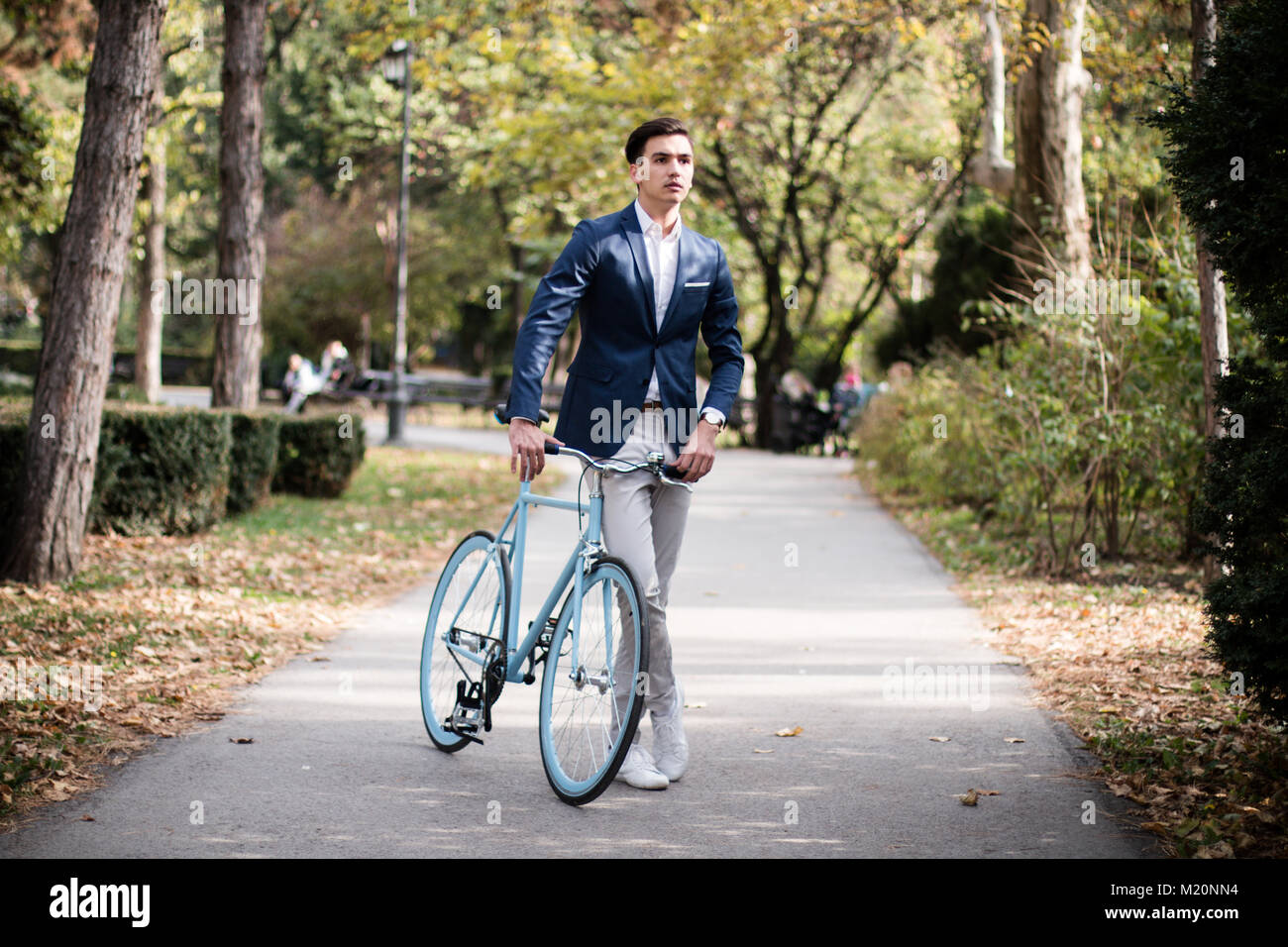 Elegant young man with blue bicycle outdoors waiting in a park Stock ...