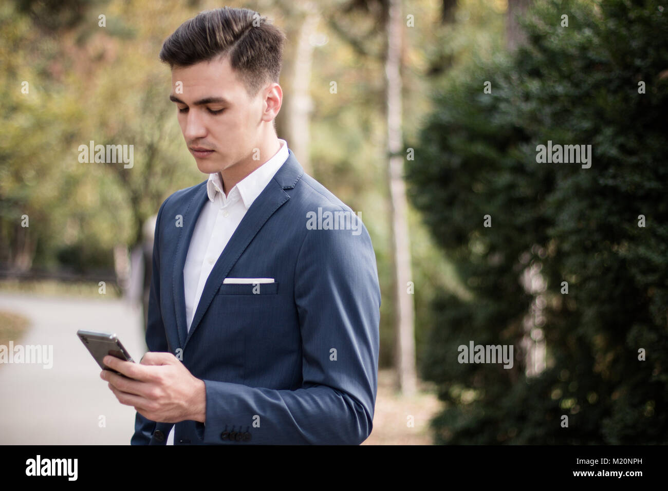 Elegant young man with smartphone outdoors in a park Stock Photo - Alamy
