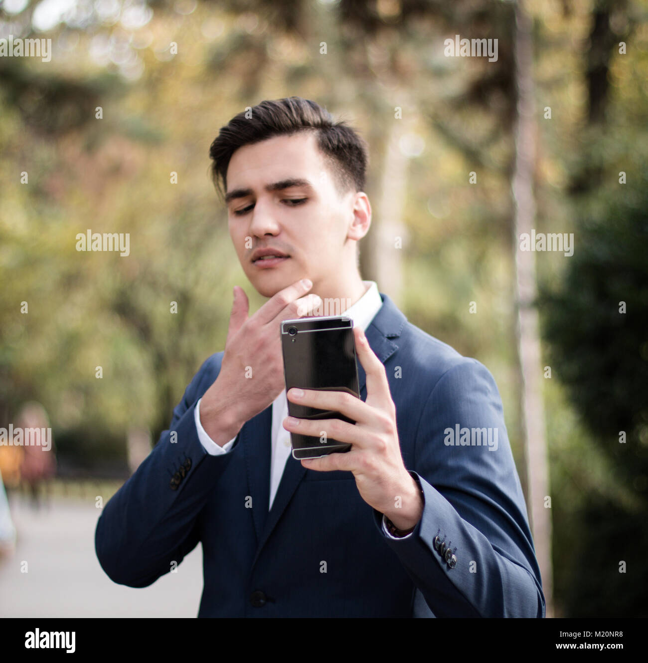 Elegant young man with smartphone outdoors in a park. Taking a picture ...
