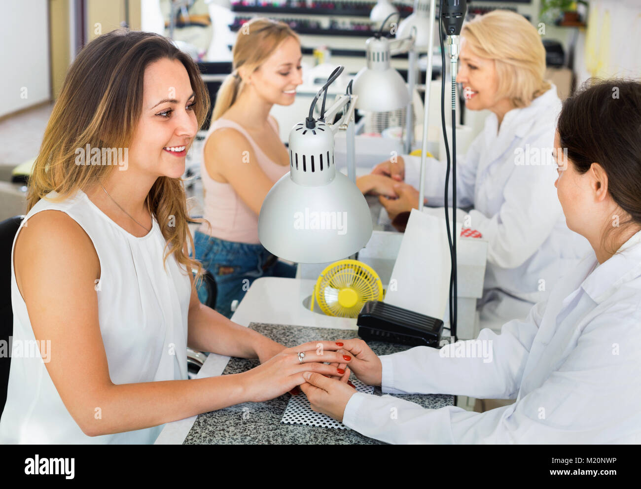 Two happy smiling positive women clients having manicure done in nail ...