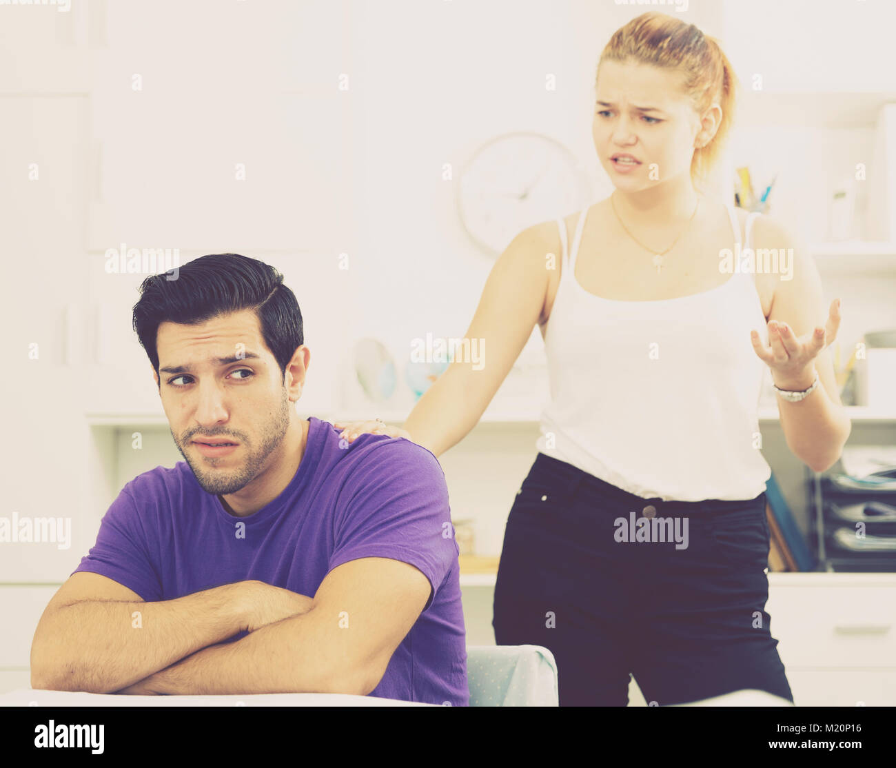Upset young man sitting at home table with disgruntled woman behind ...