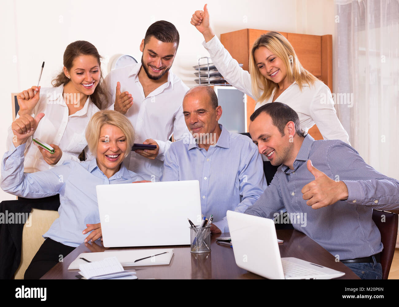 Positive colleagues looking at laptop and smiling at office Stock Photo ...