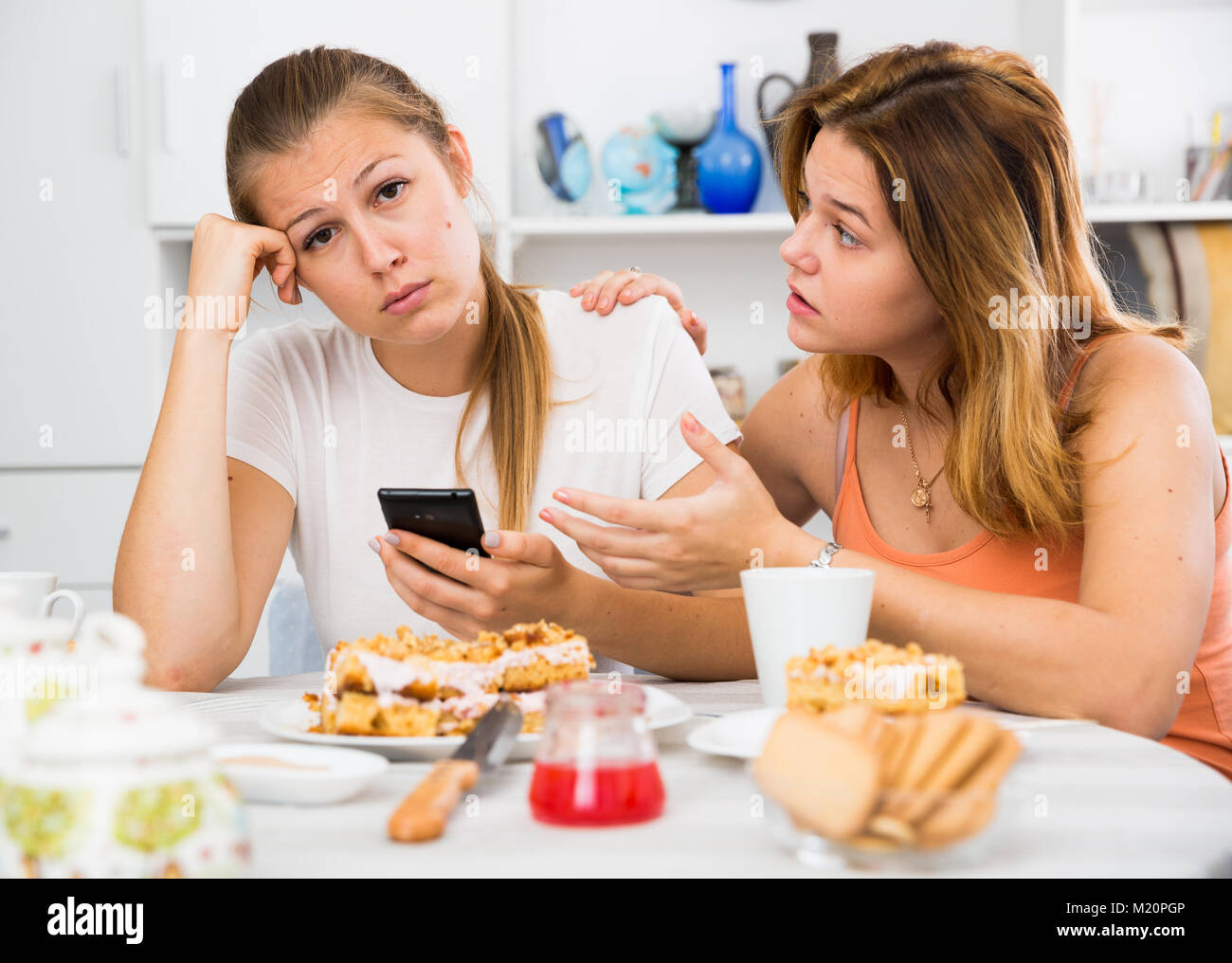 Portrait of female talking with sad girl friend with mobile at the ...