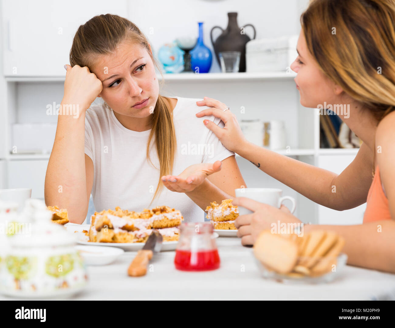 Female talking with young sad friend at the table with cake at home ...