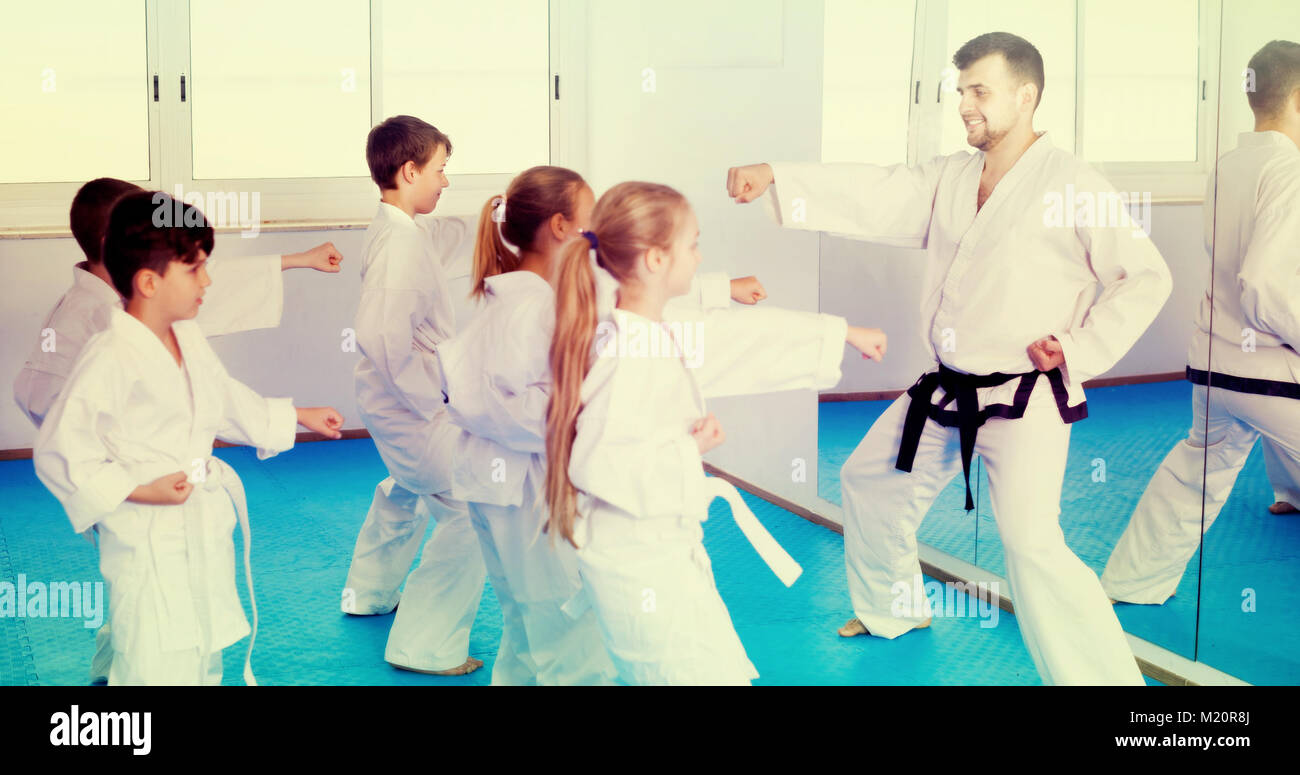 Smiling children doing karate kicks with male coach during karate class ...