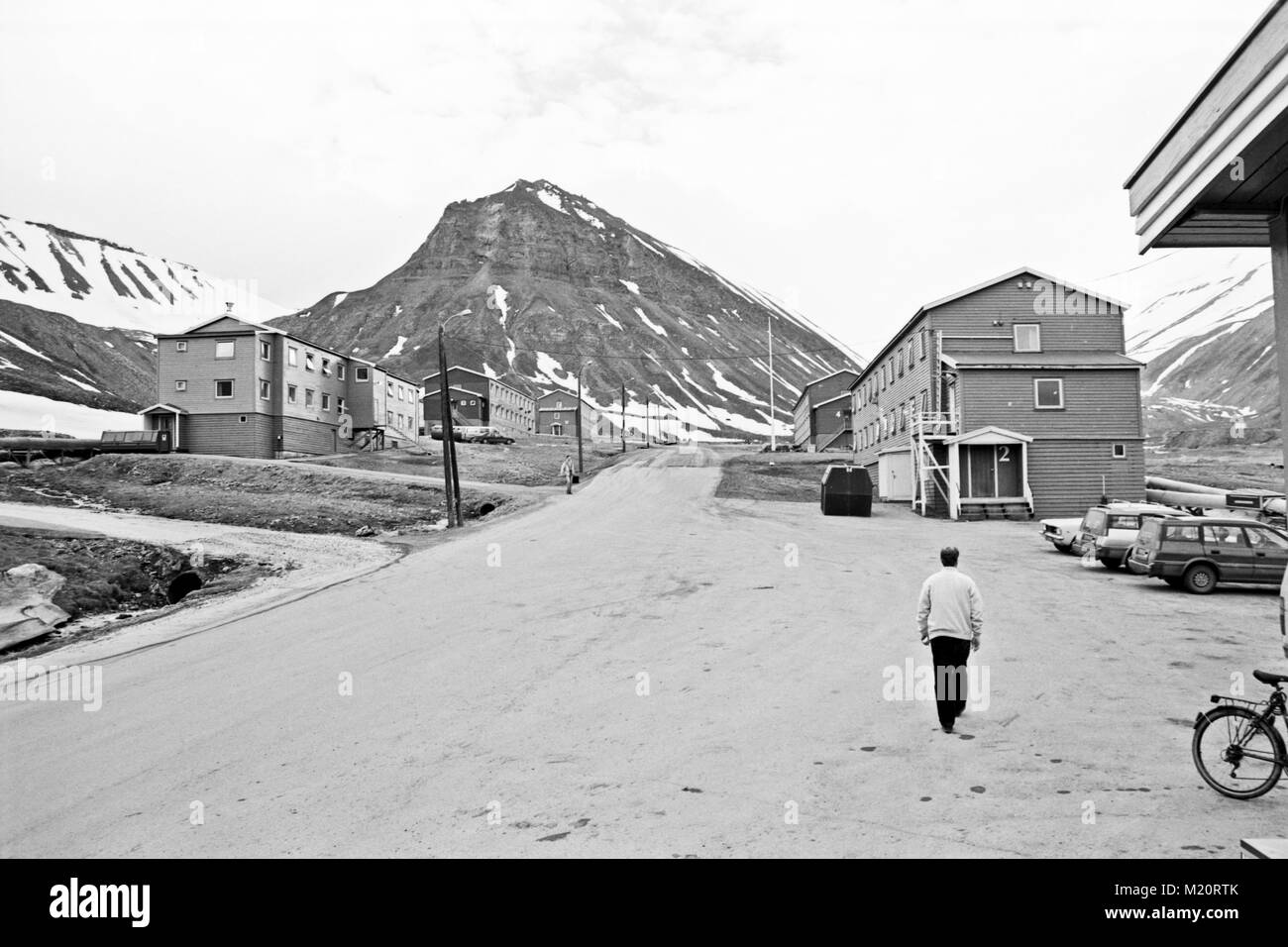 A man, back to camera, walking up a street in Longyearbyen. In the ...
