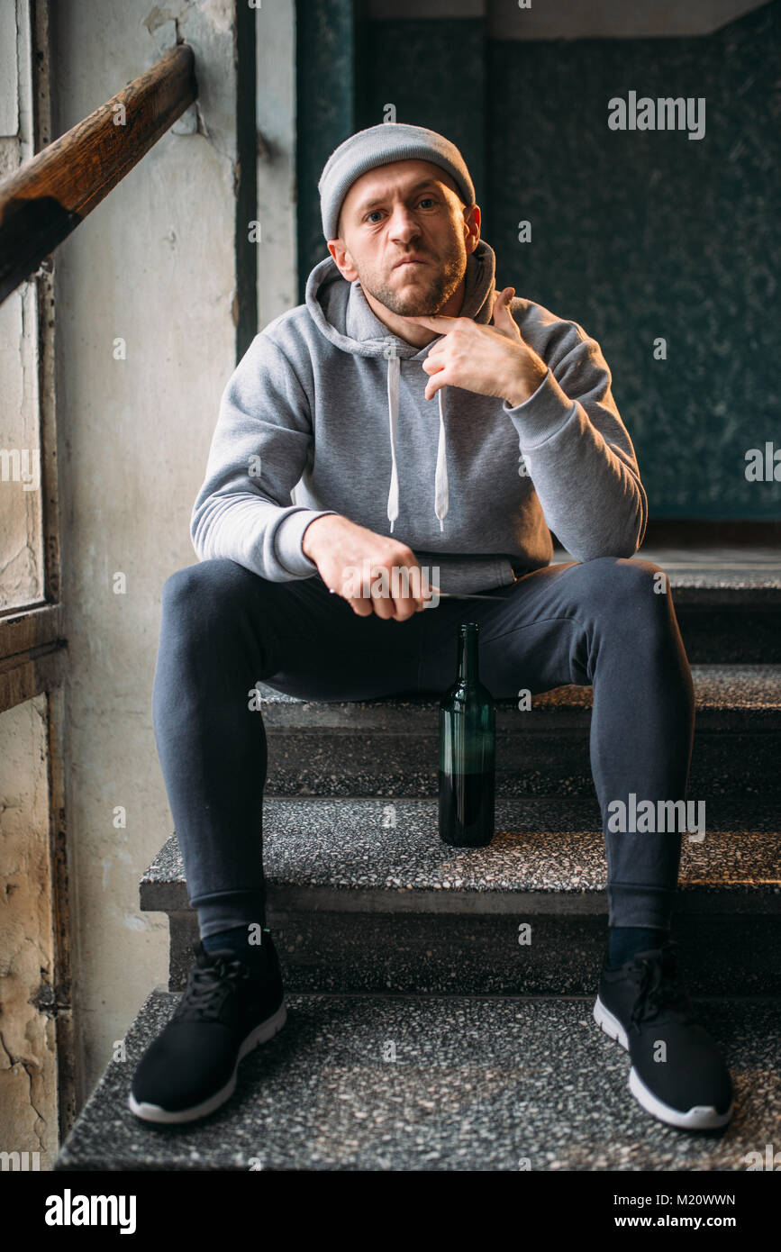 Male robber with knife sitting on the stairs. Street bandits with ...