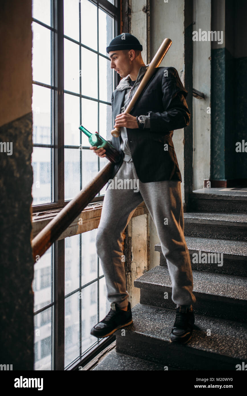 Bad guy with baseball bat and bottle of beer standing on the stairs ...