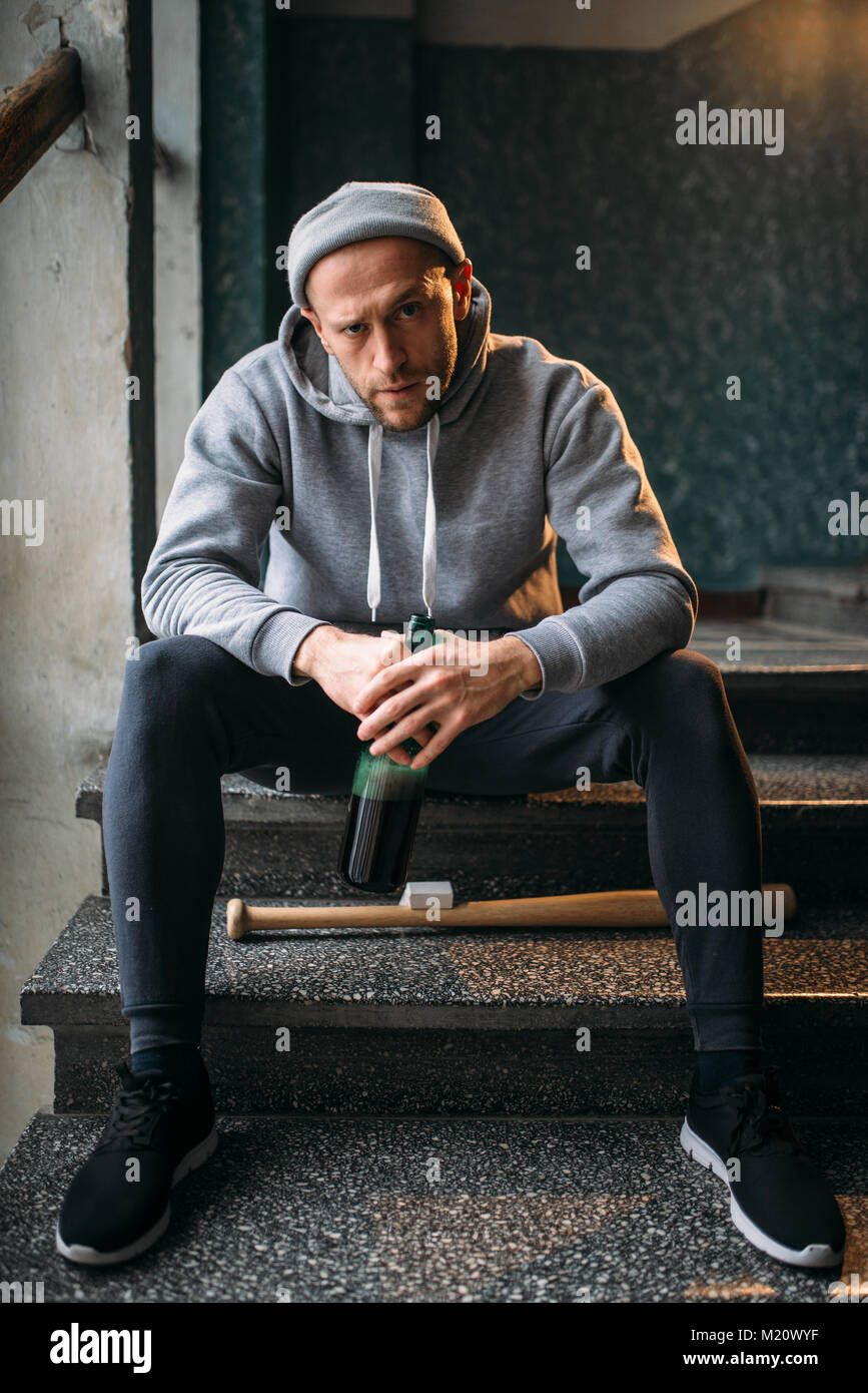 Bad guy with bottle of alcohol sits on stairs. Street robber waiting ...