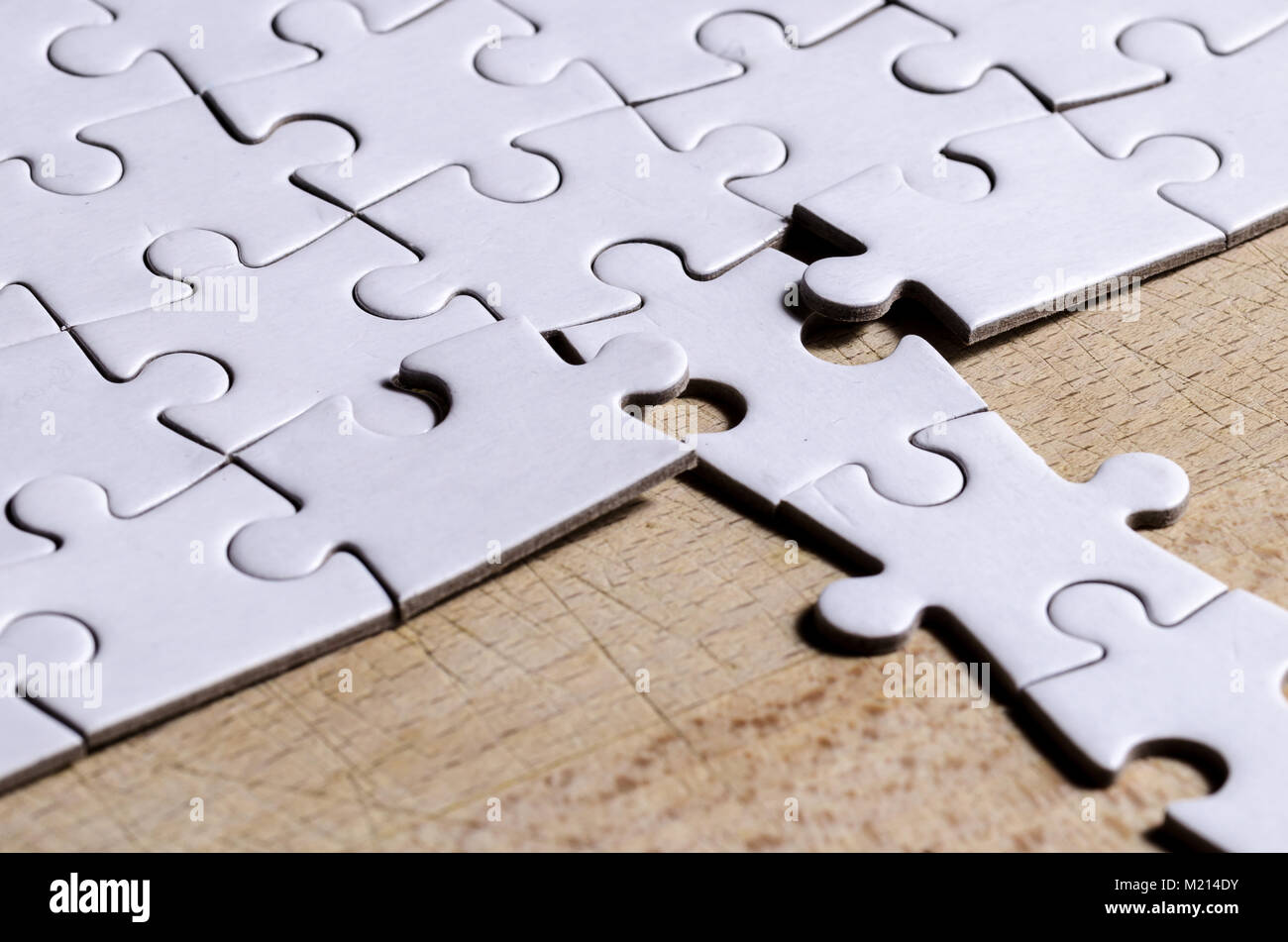 white jigsaw/puzzle with a row in wrong position, over wooden table ...