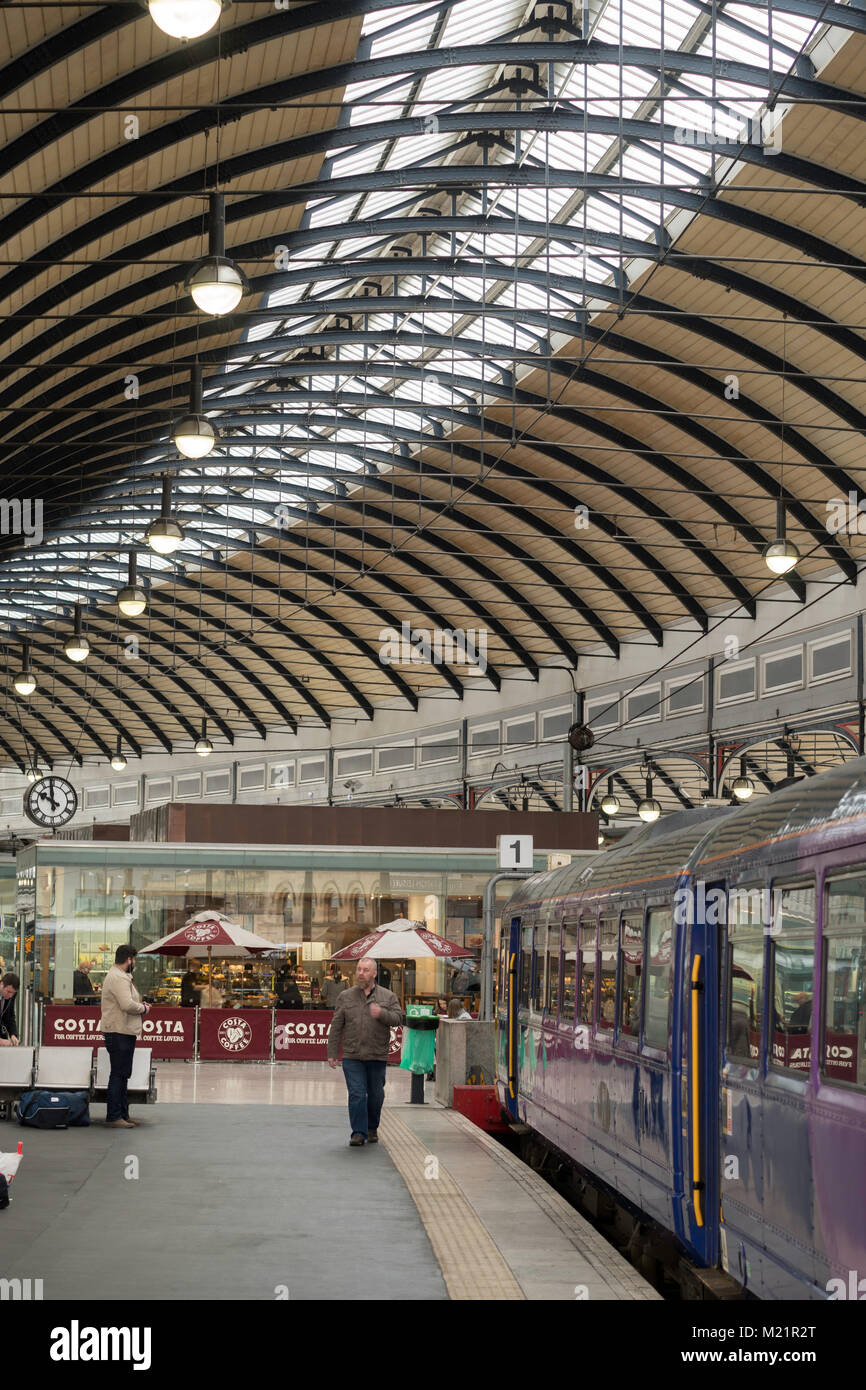 Passengers waiting to board a train beneath the long curved roof of ...
