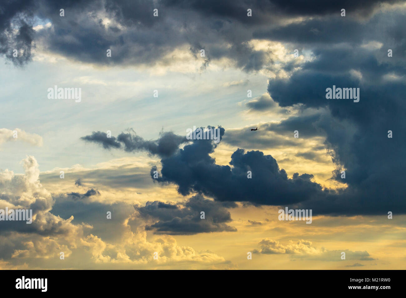 Atmospheric evening sky with clouds and a single aircraft silhouetted ...