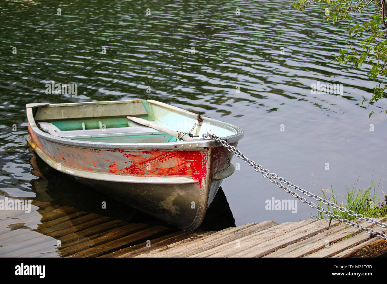 An aluminum row boat chained to the shore by a dock Stock Photo - Alamy